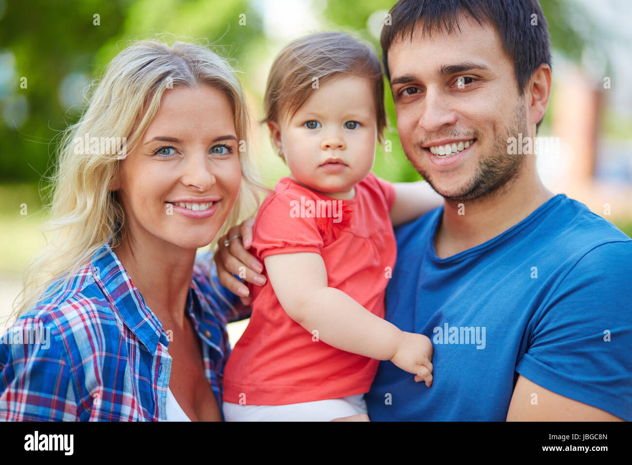 Photo of affectionate parents and their small daughter looking at ...