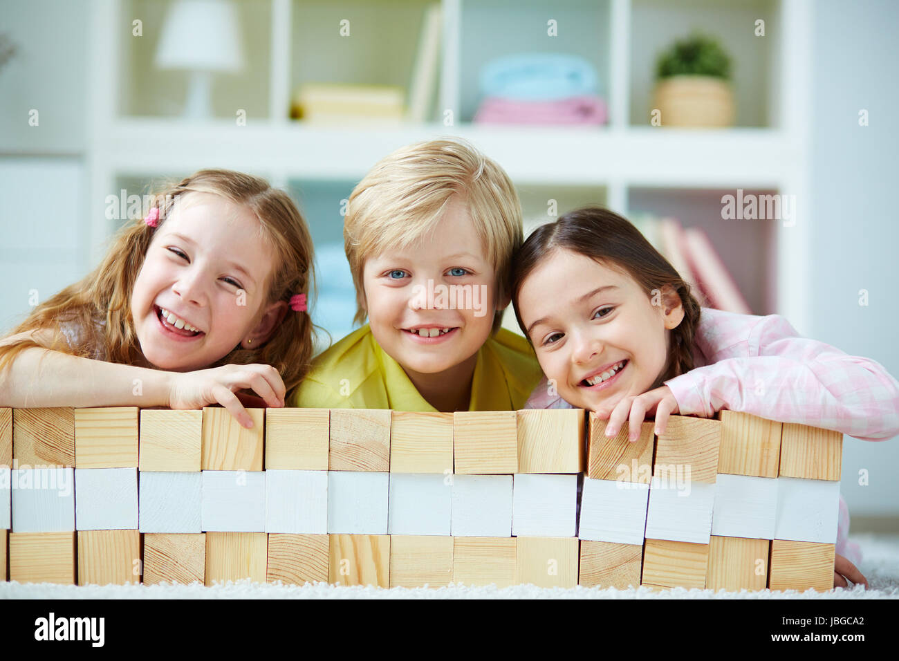 Three little friends with wooden bricks looking at camera Stock Photo ...