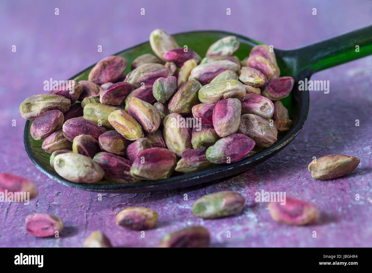 peeled pistachio nuts in a spoon, isolated, purple wooden background ...