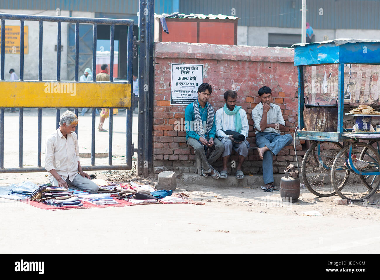 Four Indian men waiting outside the gates and wall of a large business ...