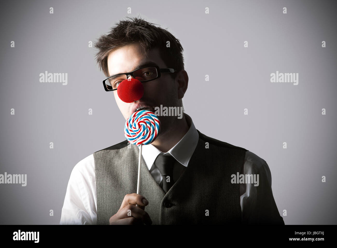 Funny portrait of young stylish man with clown nose eating lollipop ...