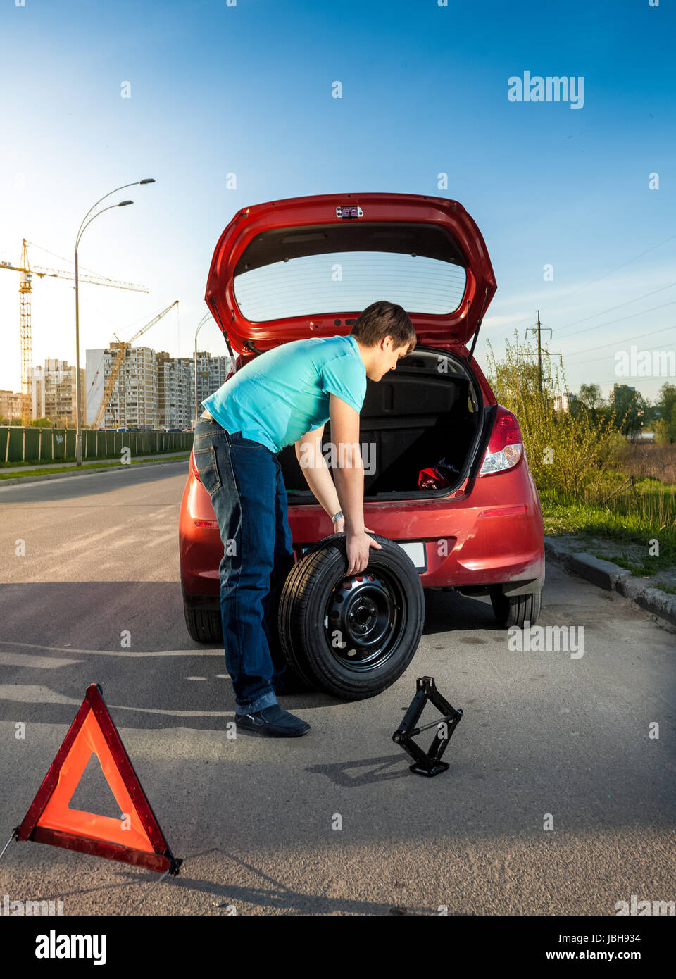 Photo of man changing punctured wheel on broken car Stock Photo - Alamy