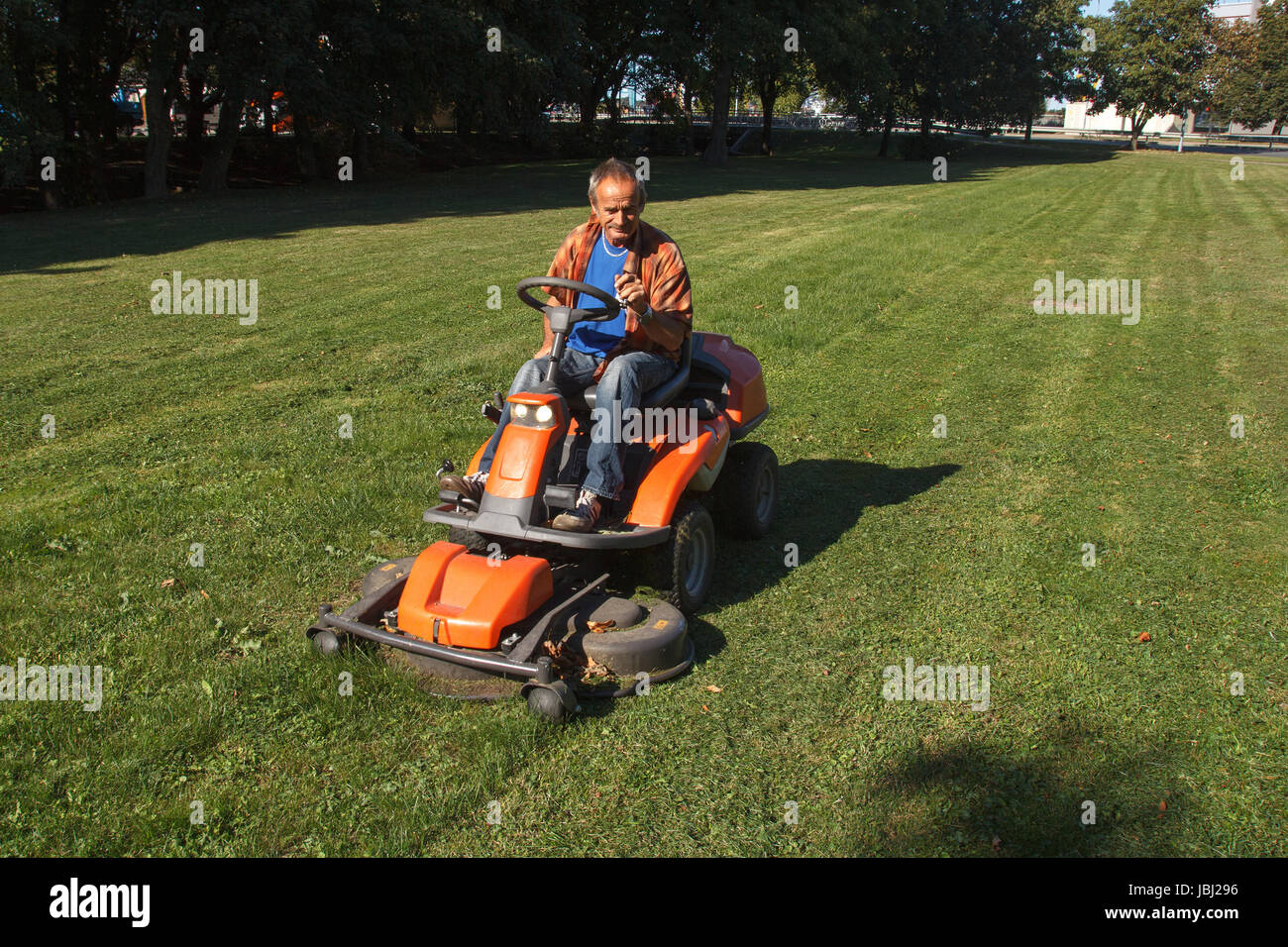 Man with ride-on lawn mower cutting grass Stock Photo - Alamy