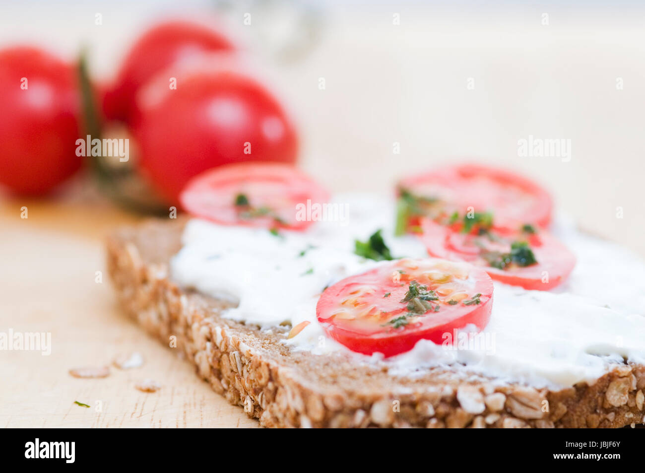 Nahaufnahme einer mit Weißkäse bestrichenen Brotscheibe sowie drei ...