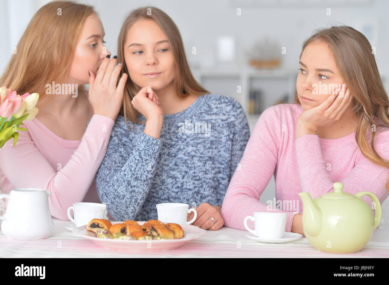 Teenage girls gossiping while sitting at table with tea and sweets ...