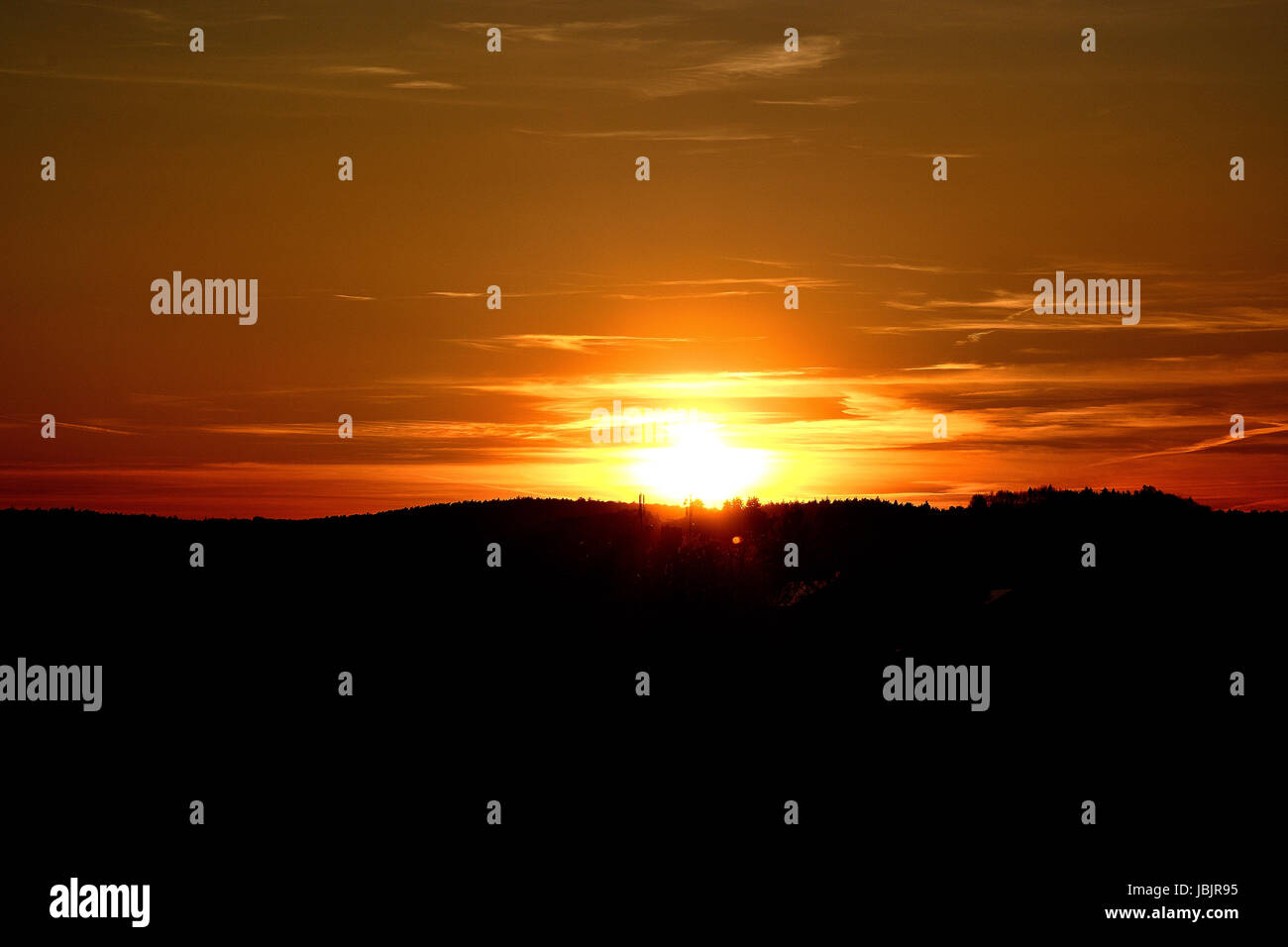 Setting sun during sunset with black landscape Stock Photo - Alamy