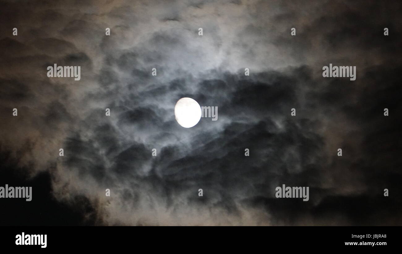 Full moon behind clouds at night . black background Stock Photo - Alamy
