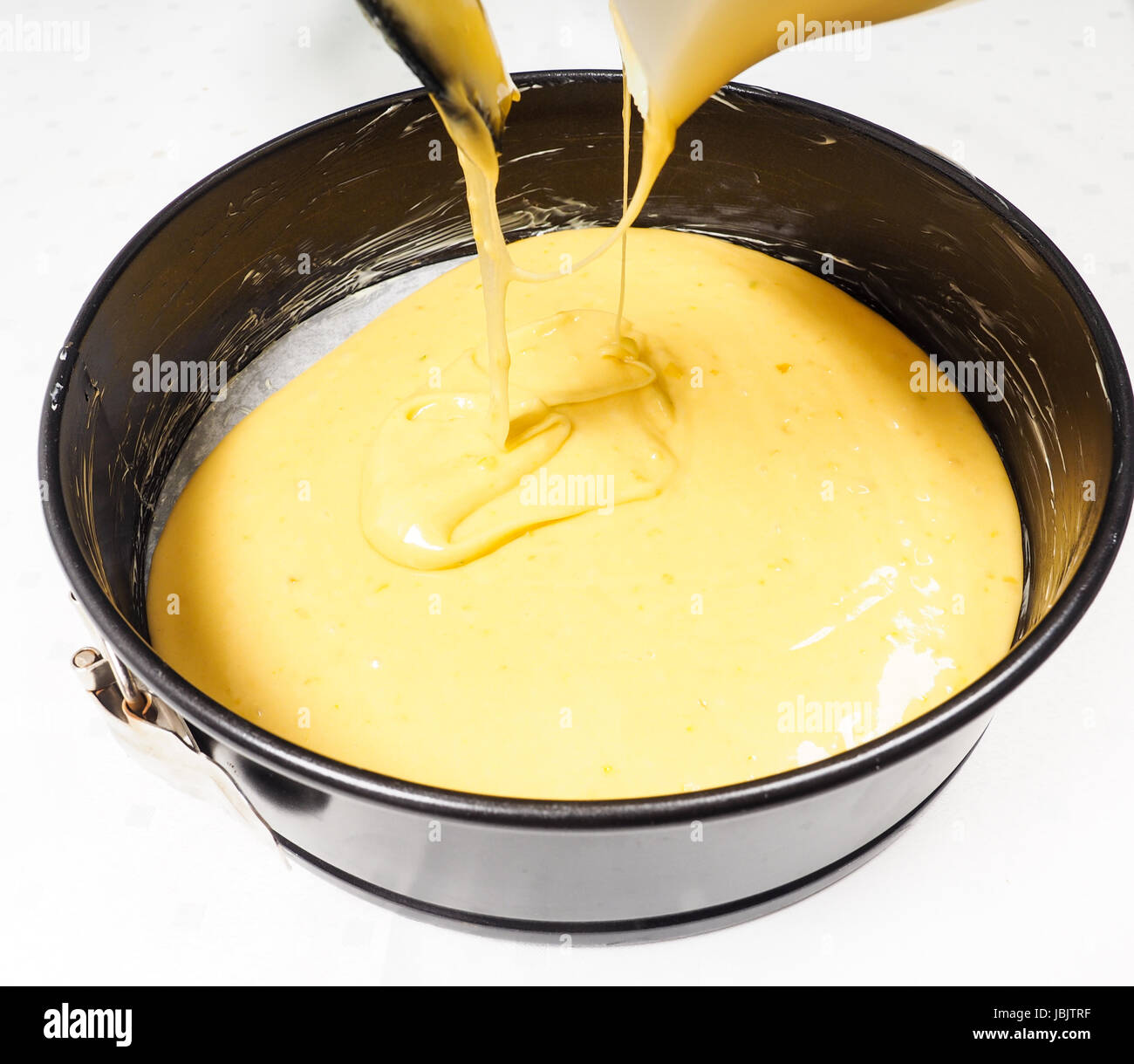 Someone adding cake mixture into a black cake ring towards white Stock ...