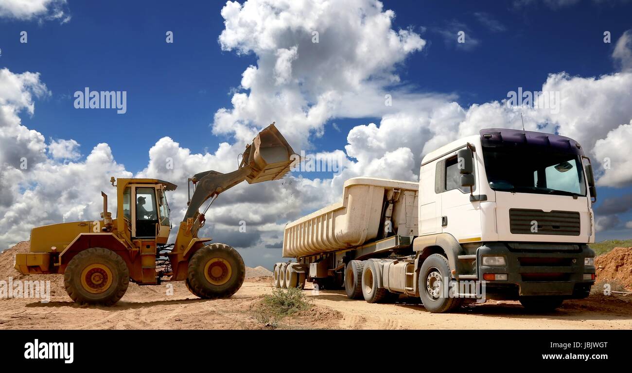 Front end loader placing stone and sand into a large truck or trailer ...