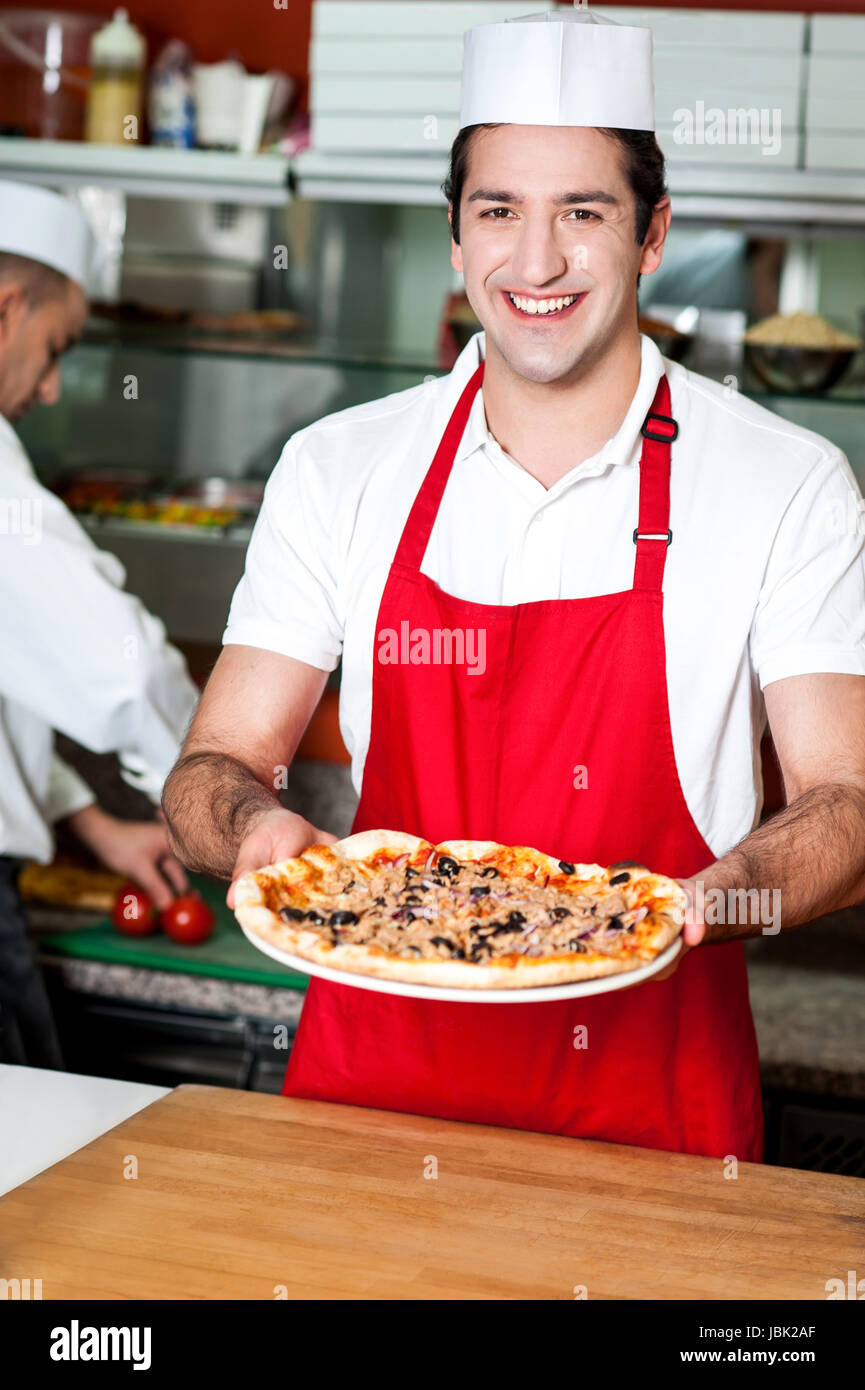 Smiling young male chef handing over pizza Stock Photo - Alamy