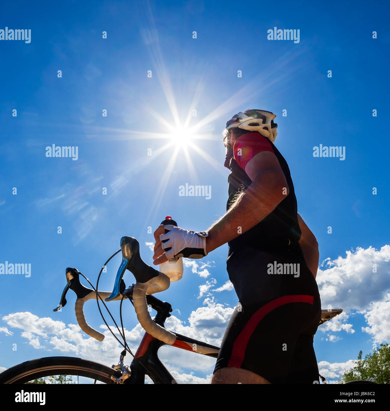 Cyclist resting and drinking isotonic drink. Backlight, sunny summer ...