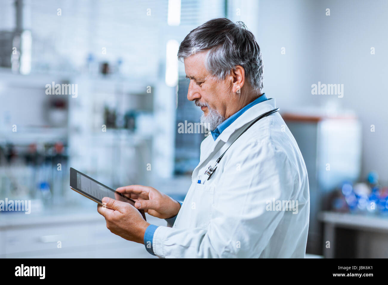 Senior doctor using his tablet computer at work (color toned image ...