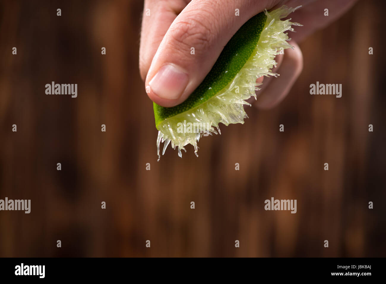 Hand squeeze lime with lime drop on dark wooden background Stock Photo ...