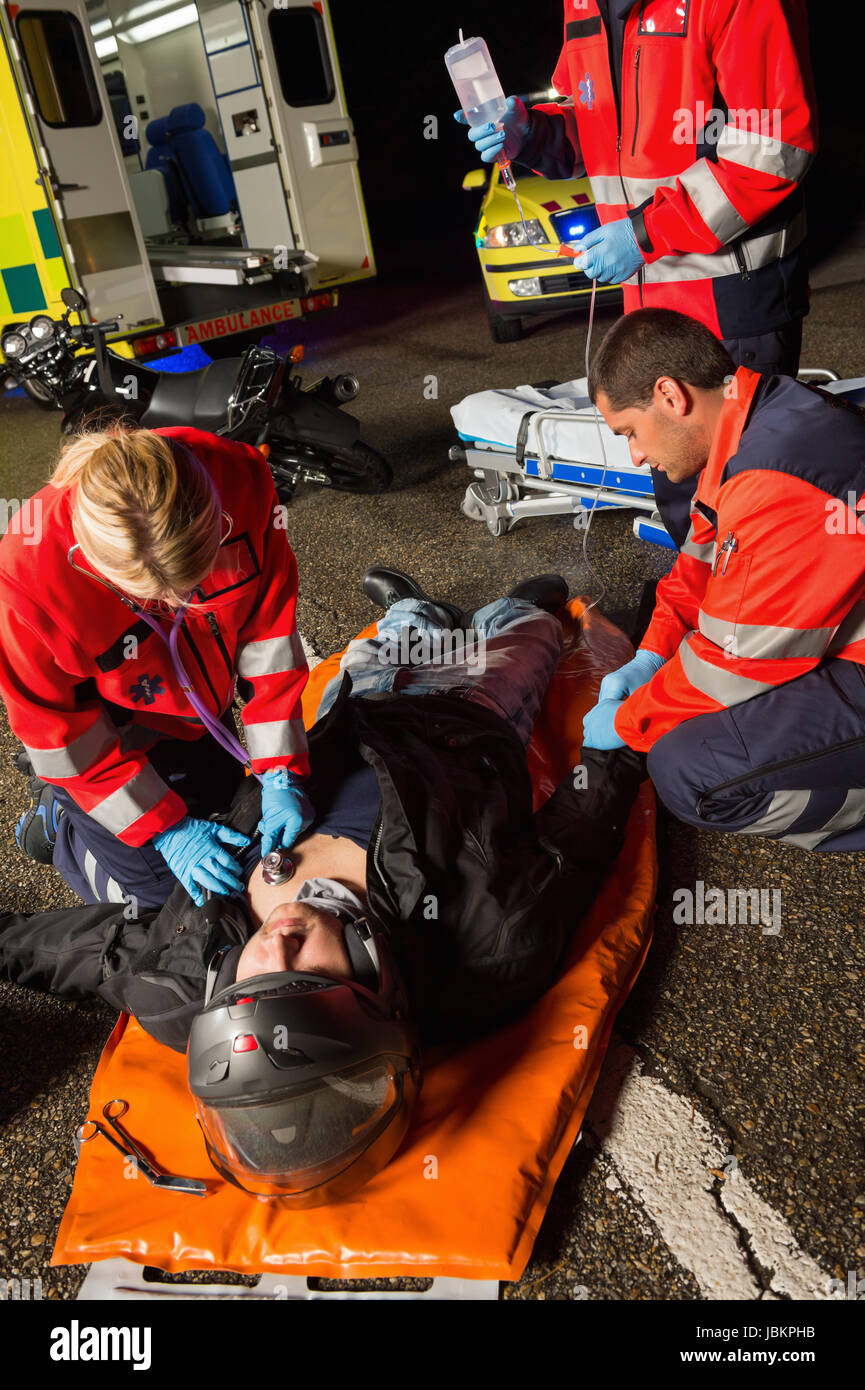 Paramedics examining injured motorcycle man driver on road at night ...