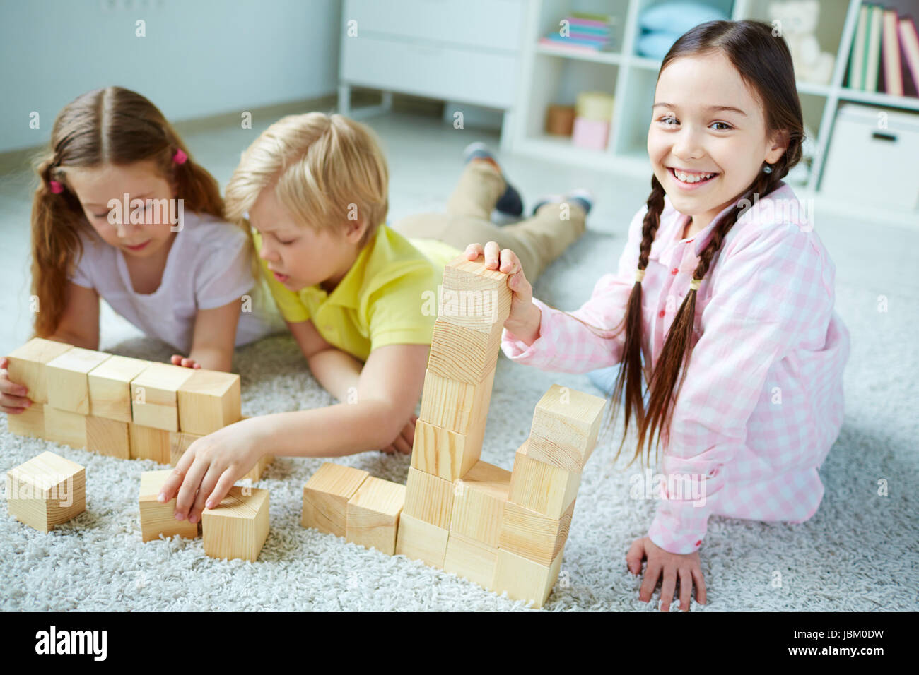 Three little friends playing with wooden bricks, happy girl looking at ...