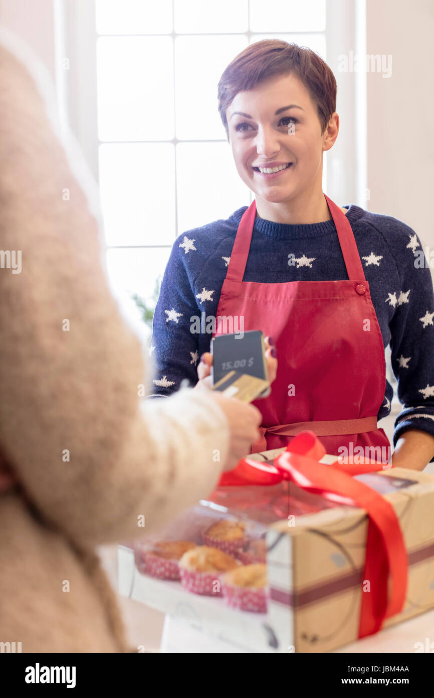 Female caterer selling box of baked pastries to woman using smart phone ...