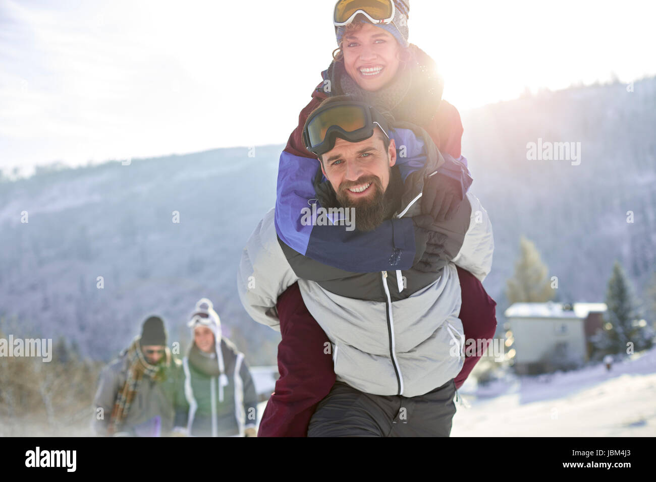 Portrait playful couple piggybacking in sunny, snowy field Stock Photo ...