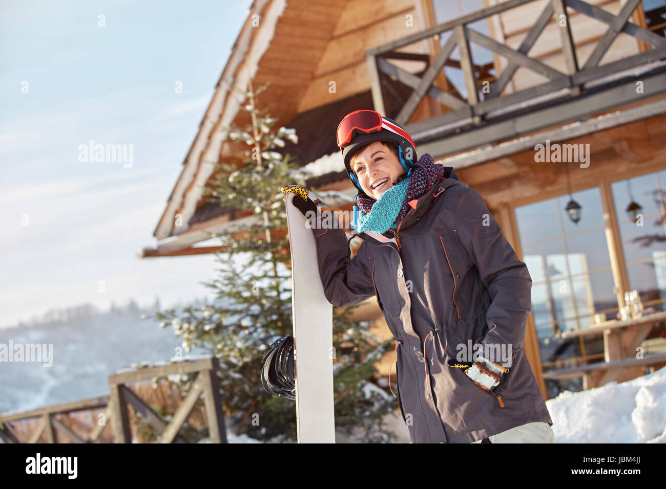 Smiling female snowboarder with snowboard outside sunny cabin Stock ...