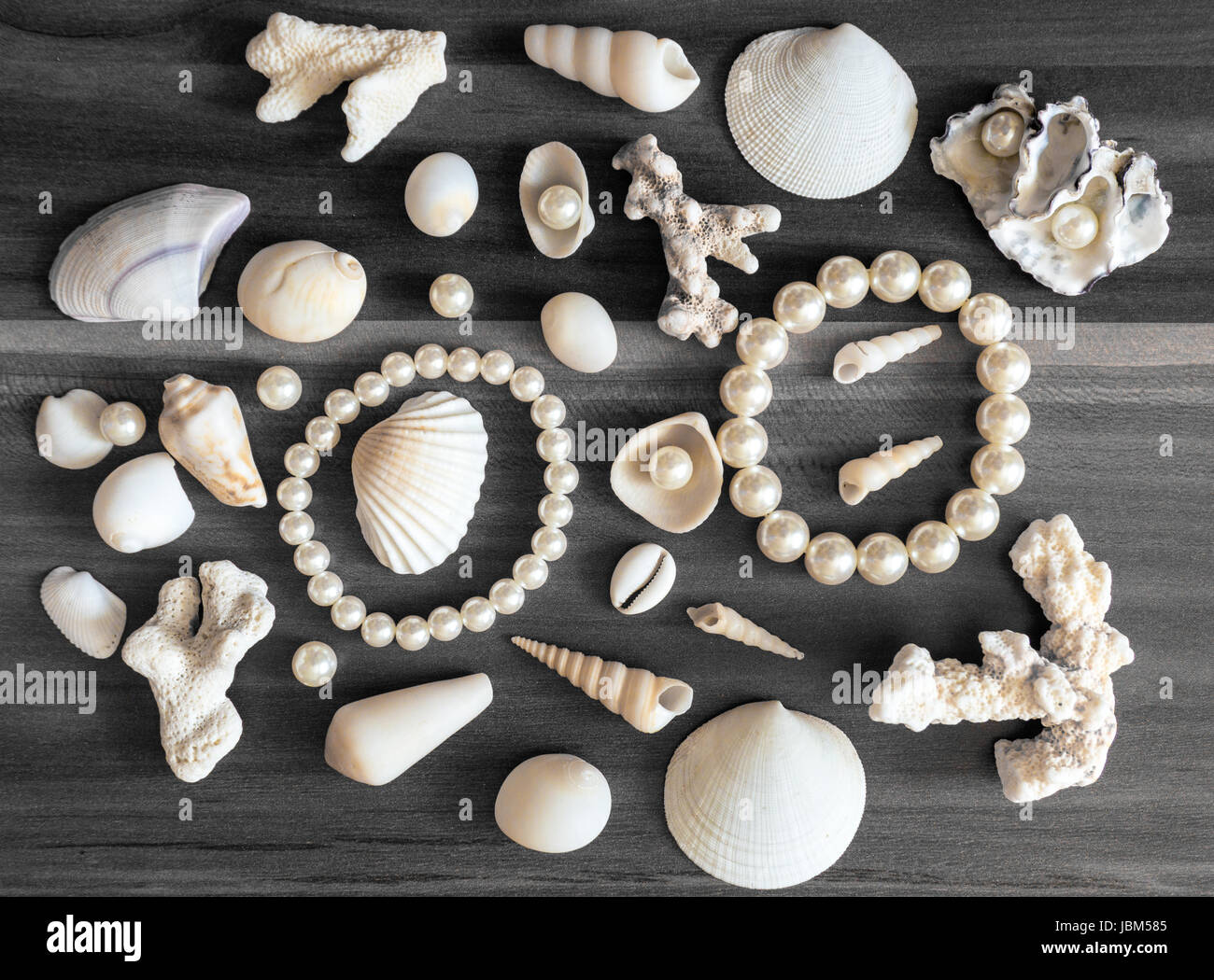 Different size and shape shells and pearls spread across a wooden ...
