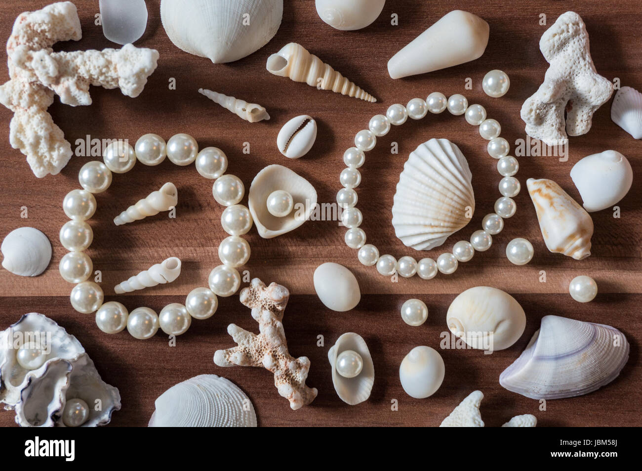 Different size and shape shells and pearls spread across a wooden ...