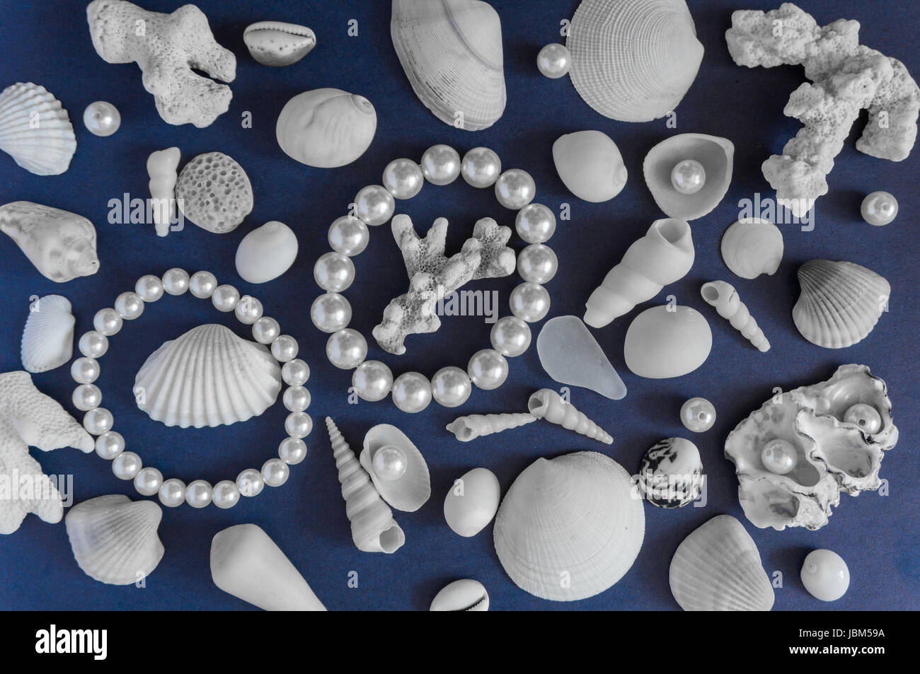 Different size and shape shells and pearls spread across a blue ...