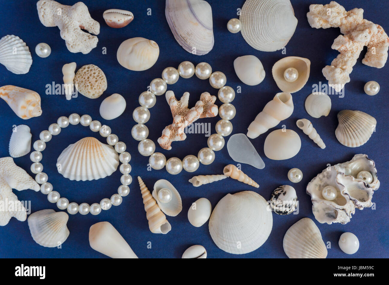 Different size and shape shells and pearls spread across a blue ...