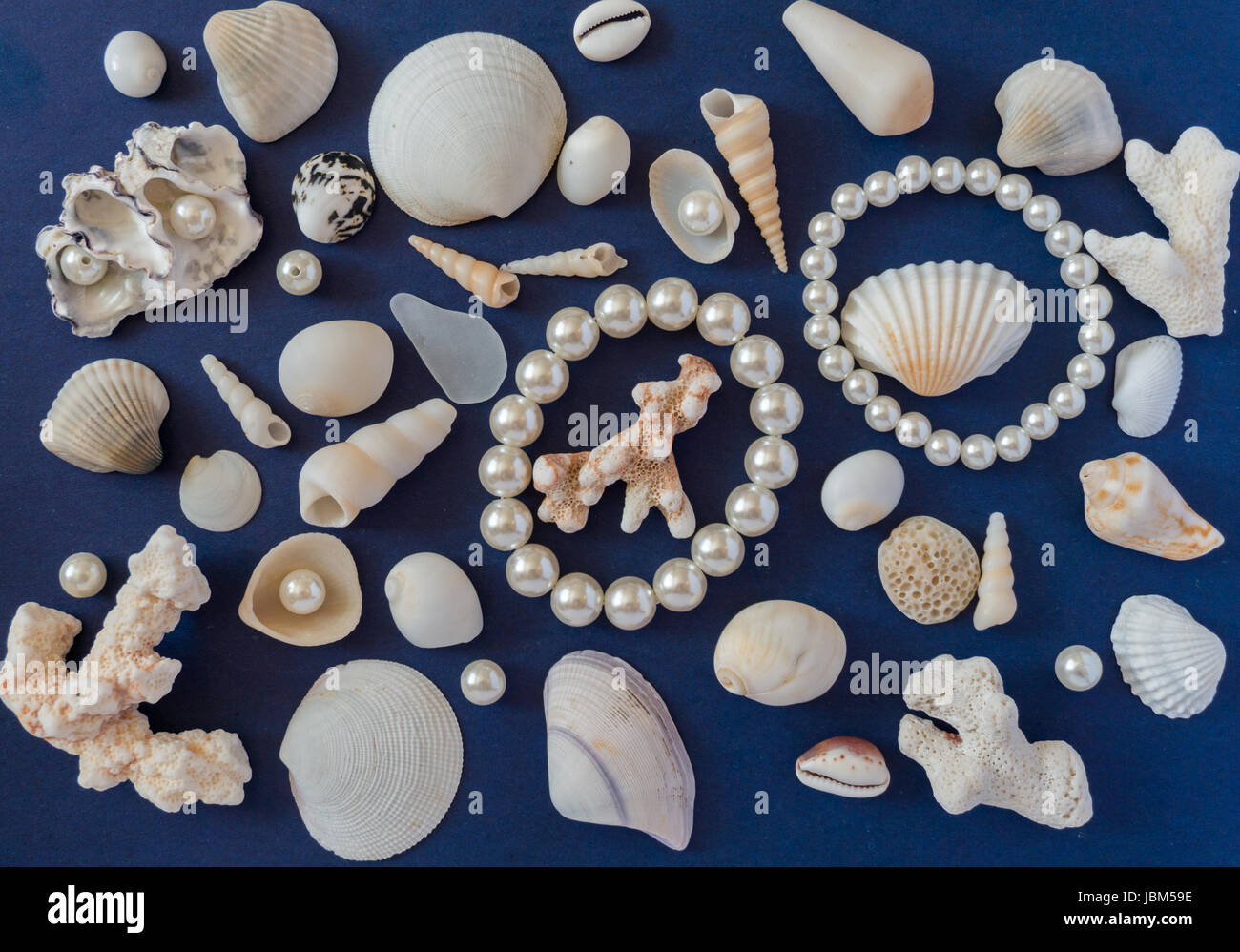 Different size and shape shells and pearls spread across a blue ...