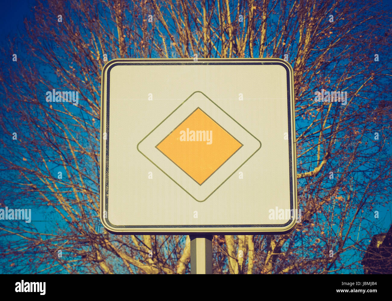 Vintage retro looking Right of way sign over blue sky with trees Stock ...