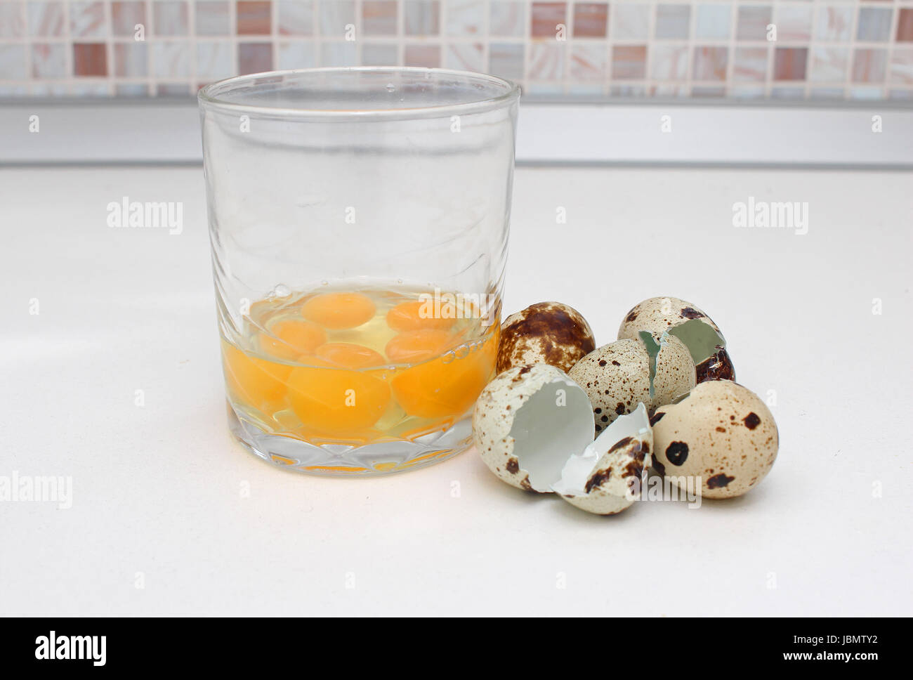 Broken quail eggs in transparent glass with empty shells next to it ...