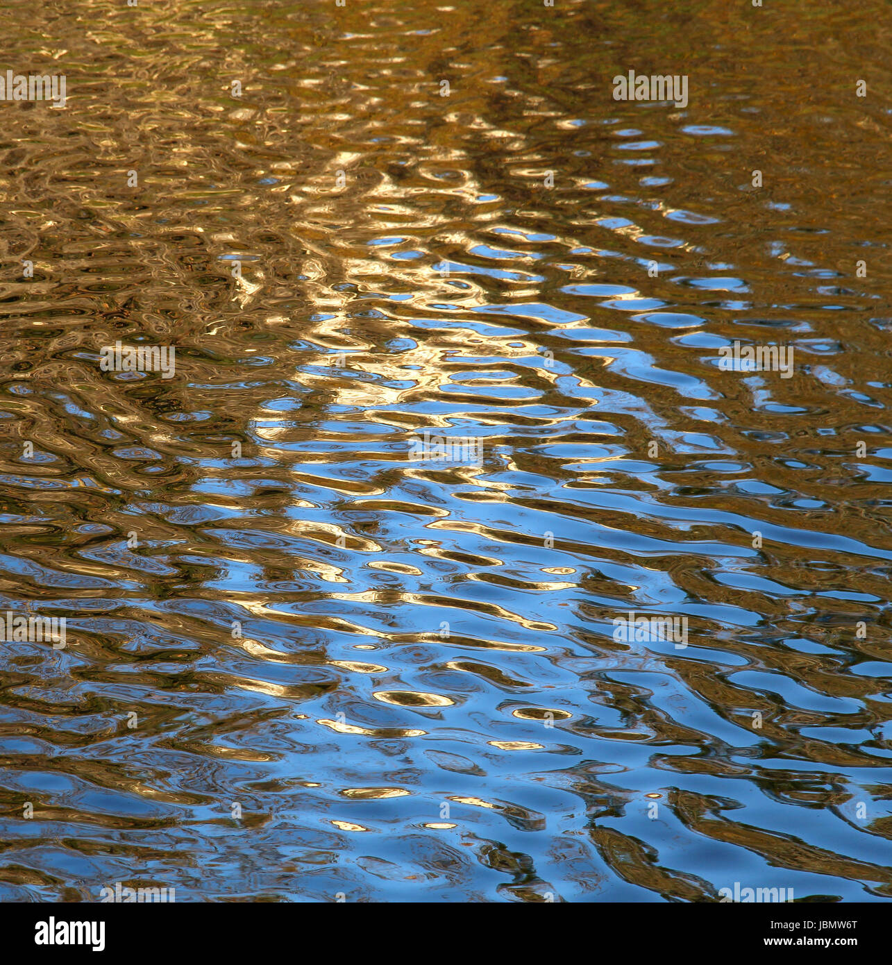 Gold and blue evening light reflects on ripples on lake surface, use as ...