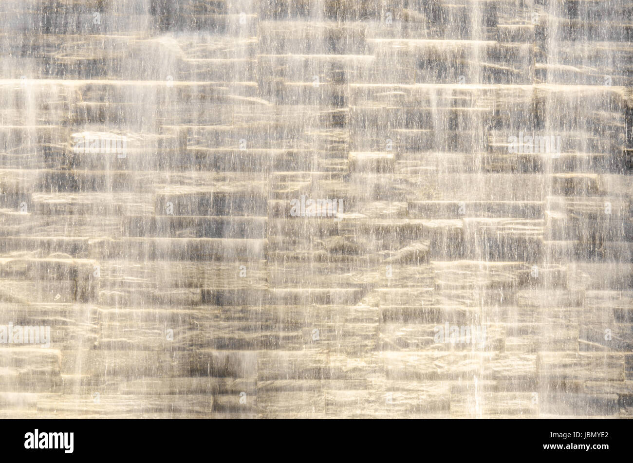 Falling water stream against stone wall rough texture with night ...