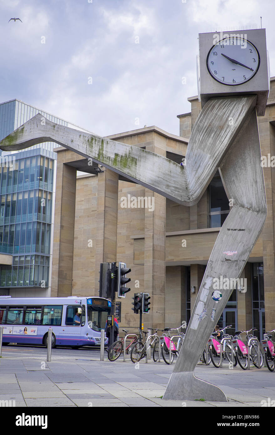 a stainless steel statue of a running pair of legs, with a cube clock ...