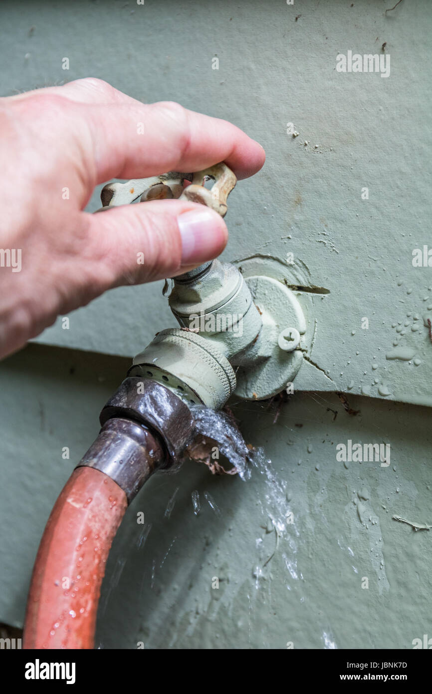 Vertical photo of a mature caucasian male hand turning outdoor faucet ...