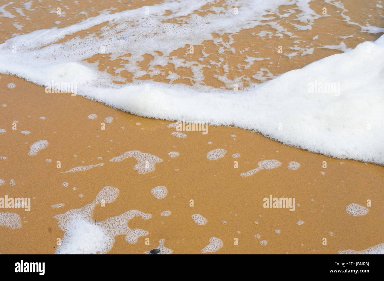 Foam breaking on beach in close up Stock Photo - Alamy
