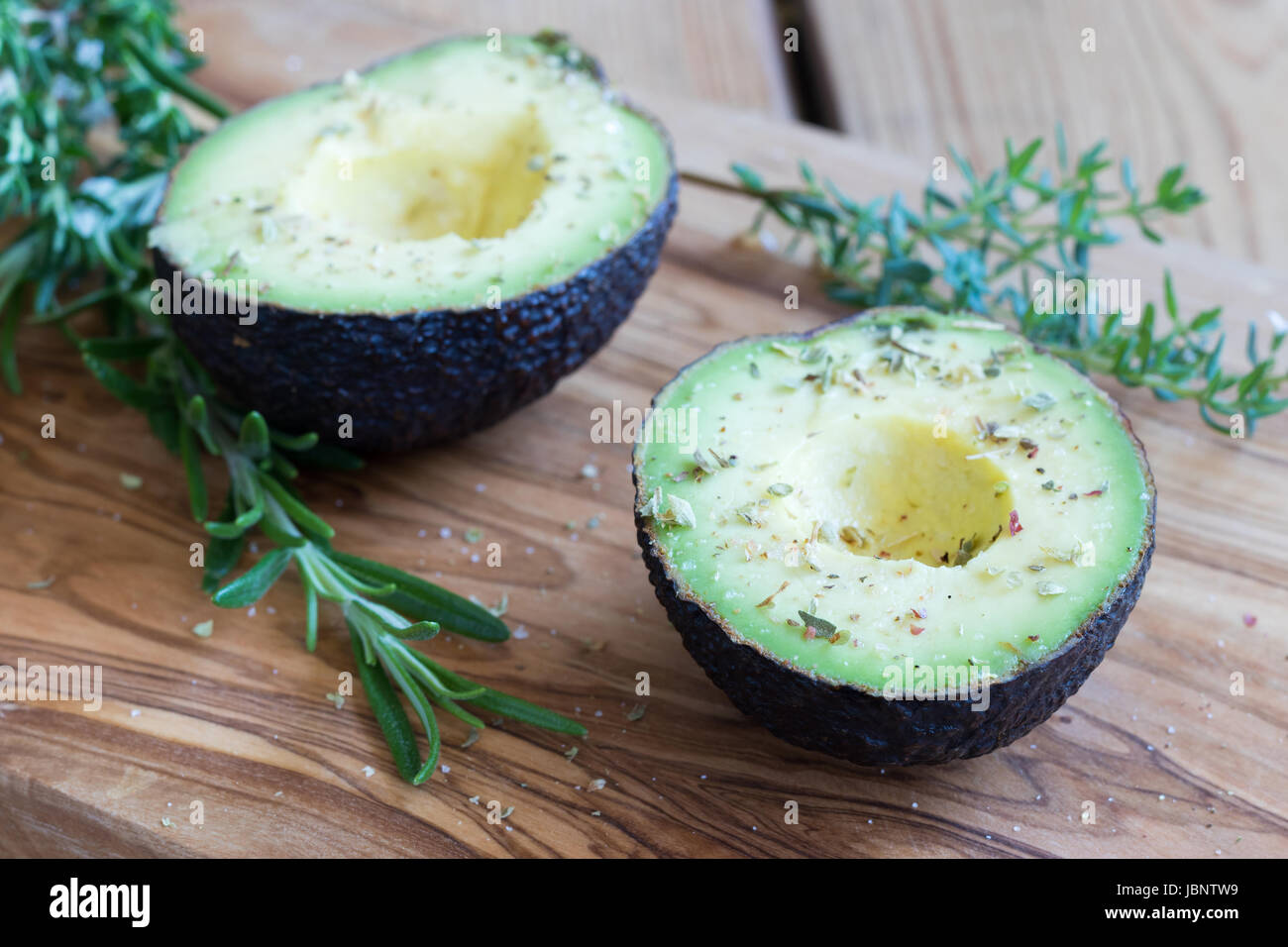 Two halves of avocado with salt, pepper and herbs on a wooden ...