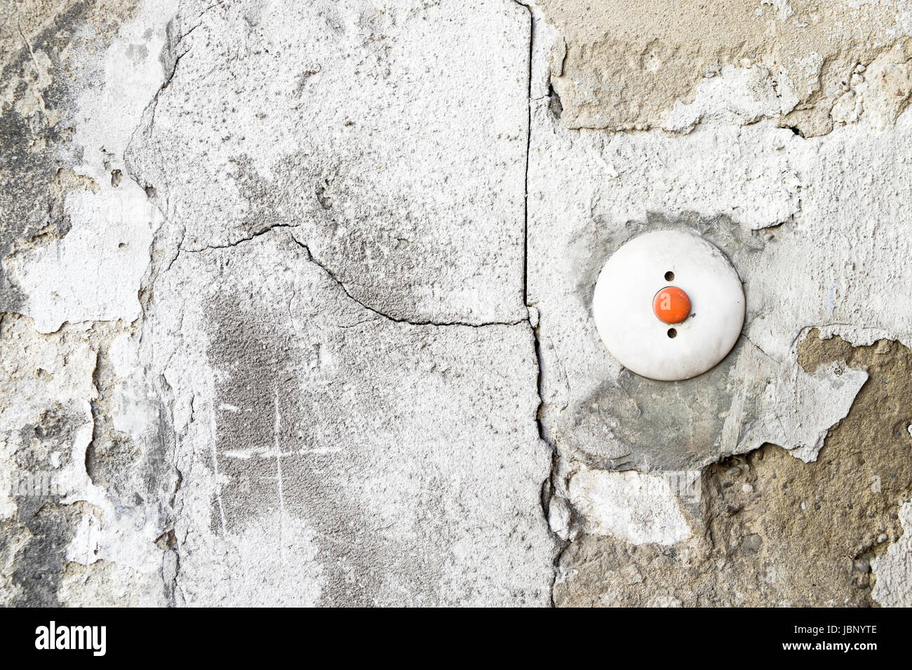 A retro red doorbell buzzer, surrounded by cracked concrete and flaking ...