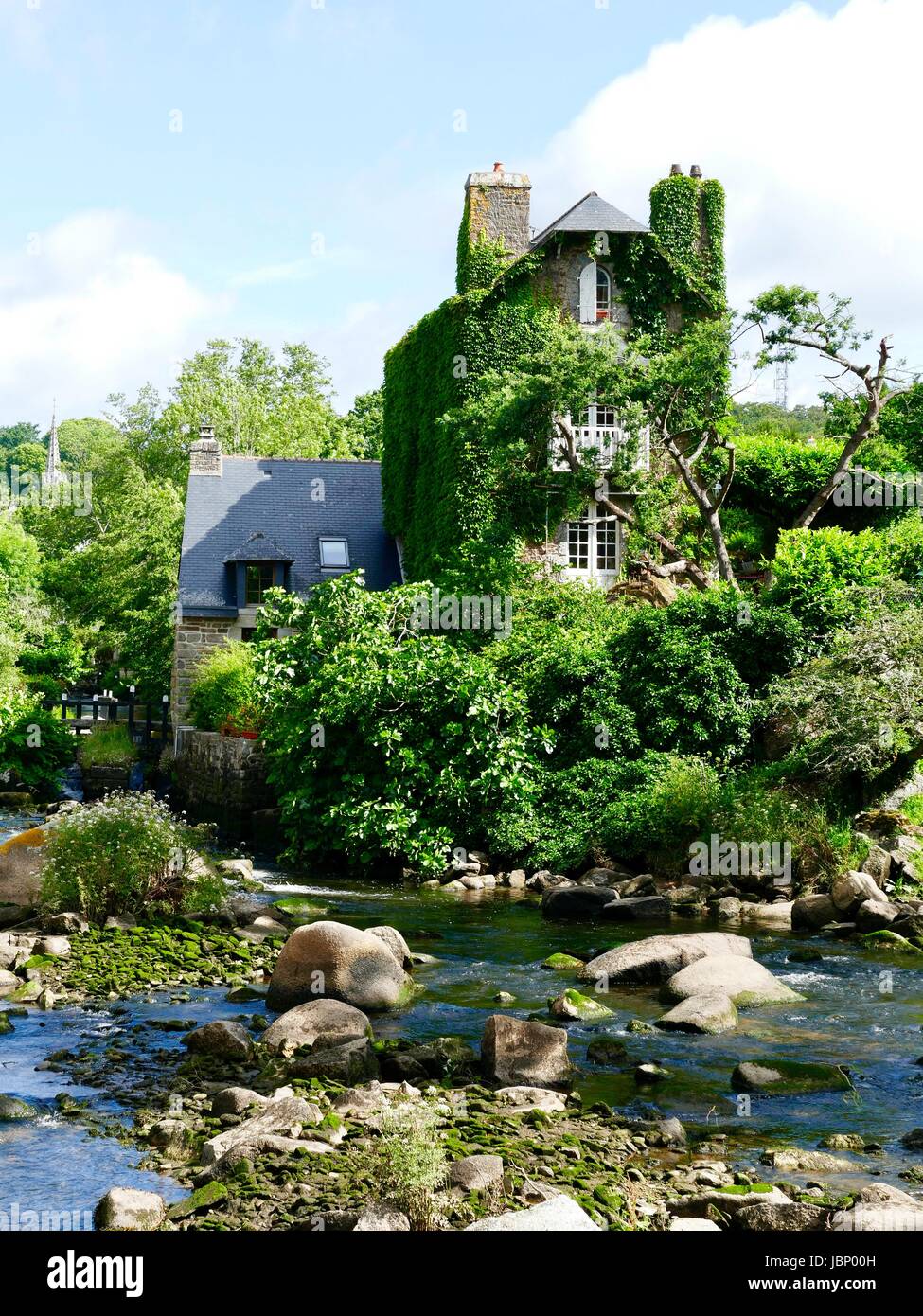 River flowing over large rocks with old, ivy covered building. Pont ...