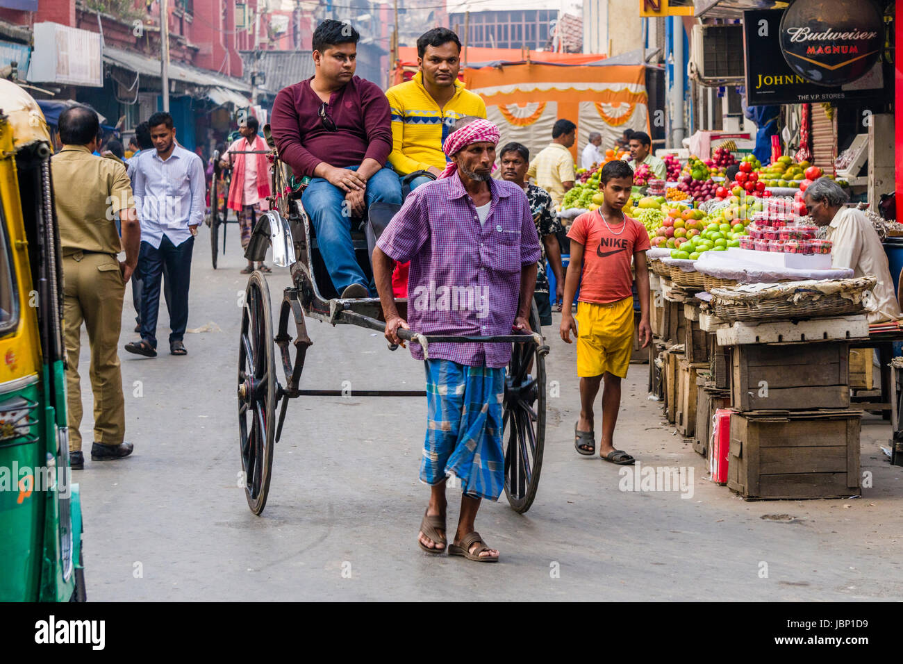 A man is pulling a rickshaw, transporting two people, on a road in the ...