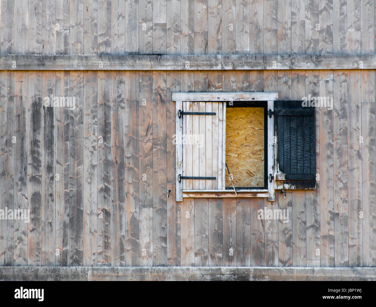 Burnt window shutter half-open in weather worn dilapidated building of ...