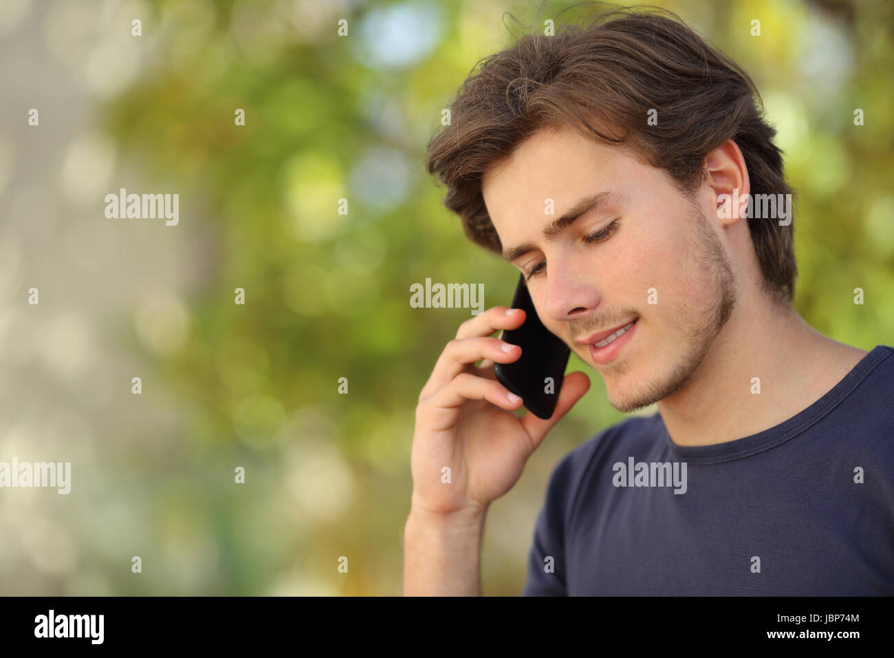 Handsome man talking on the mobile phone outdoor with green background ...