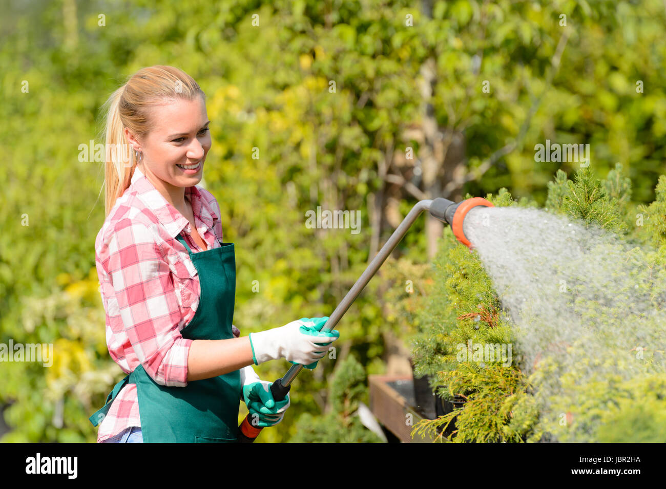 Garden center woman worker watering plants with hose smiling sunny ...