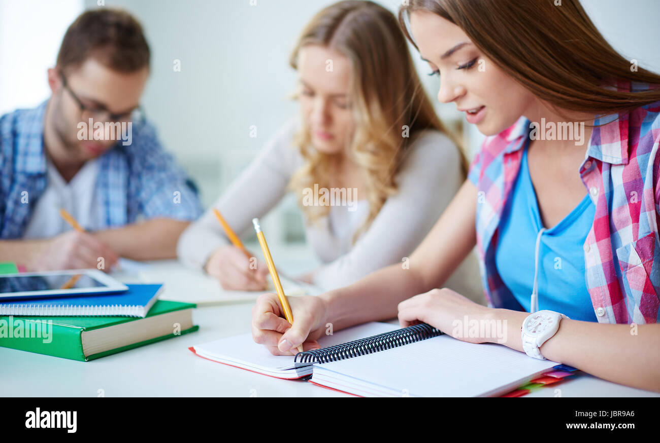 Smart girl and her groupmates on background carrying out written task ...