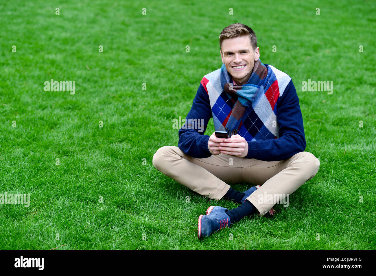 Casual man operating phone. seated in park Stock Photo - Alamy