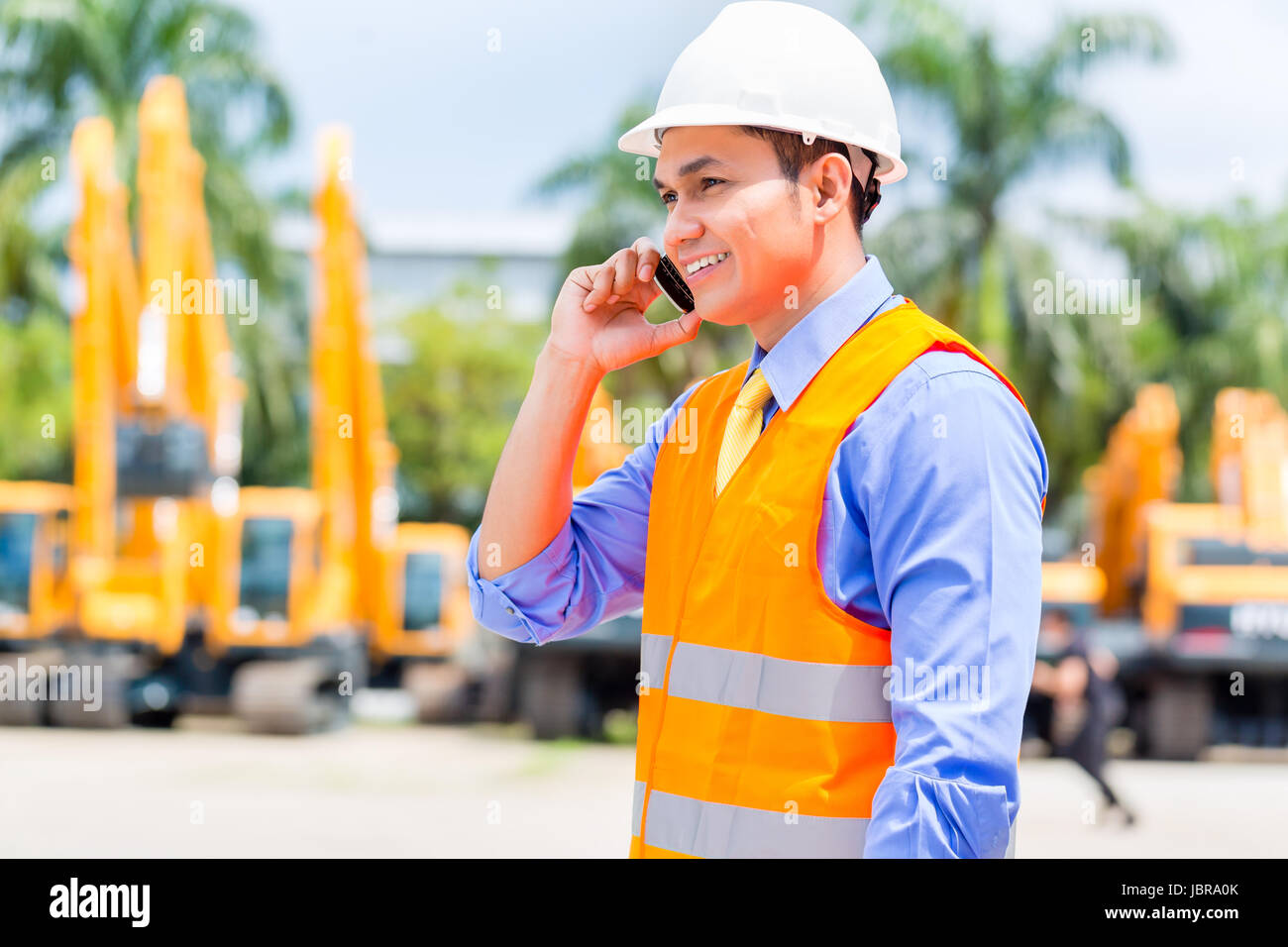 Asian foreman telephoning with mobile phone of building site or mining ...