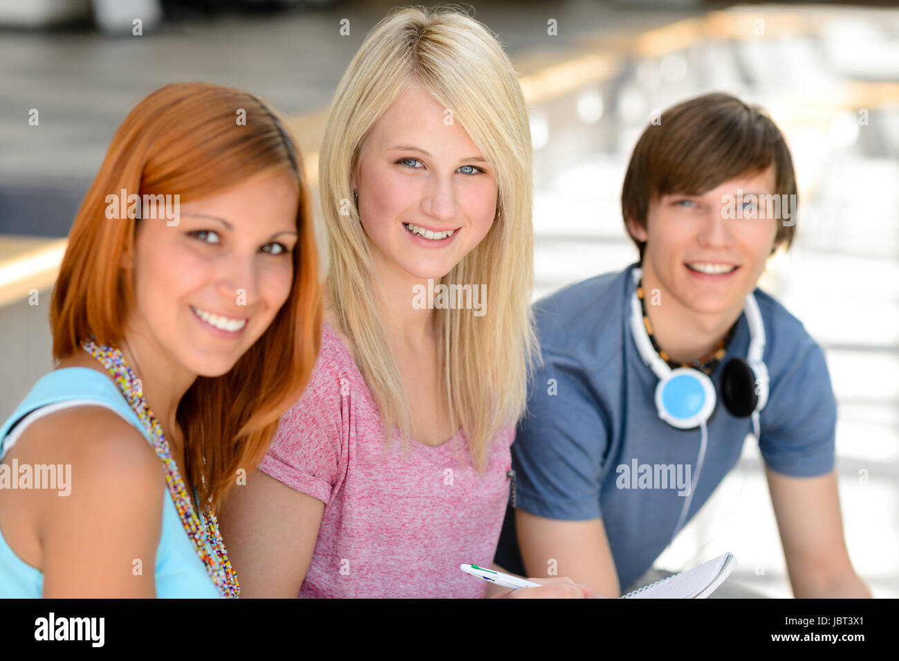 Three smiling college student friends sitting together looking at ...