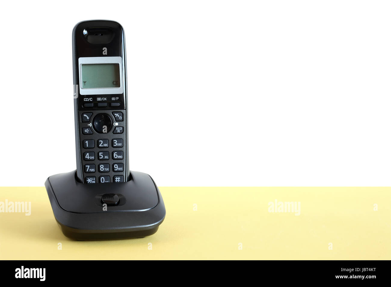 Modern black wireless telephone on yellow surface against white ...