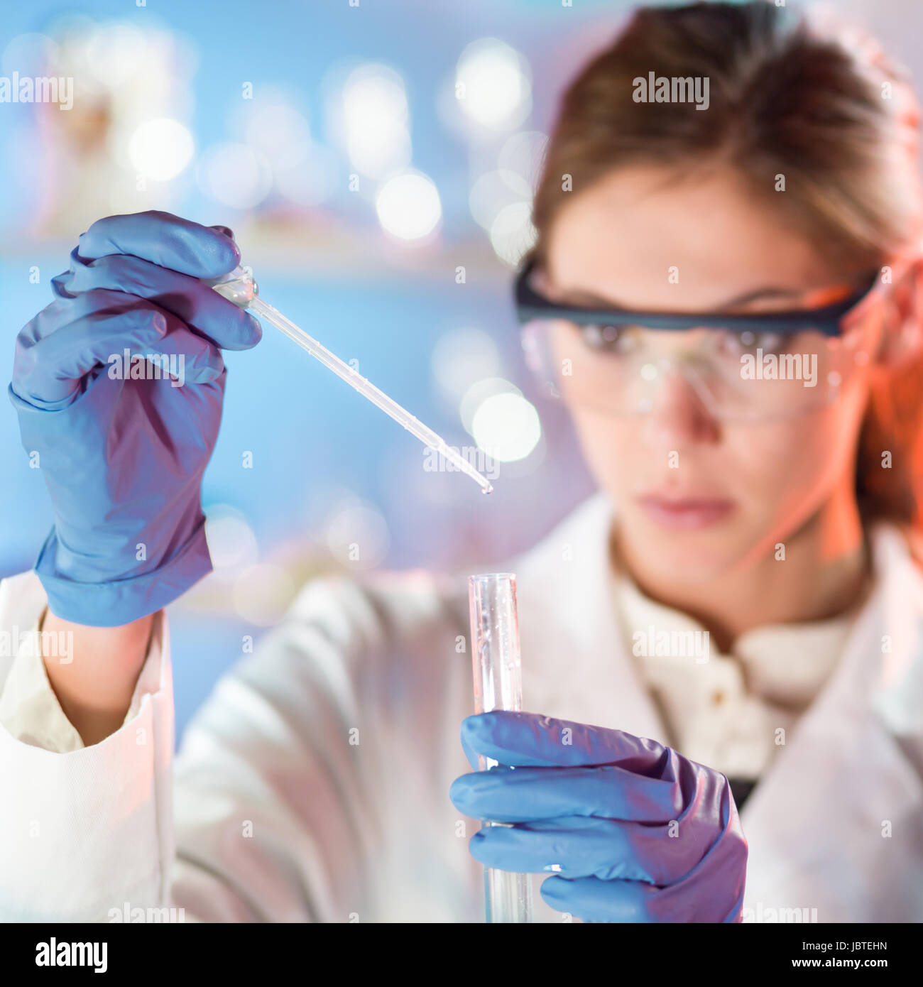 Focused young life science professional pipetting solution into the ...