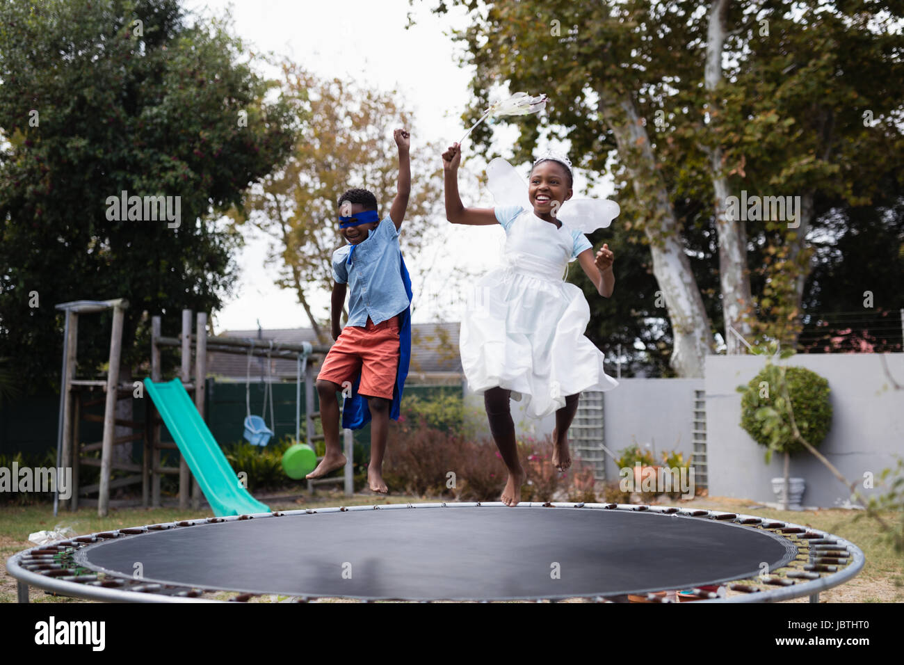 Playful siblings in costumes enjoying on trampoline at lawn Stock Photo ...