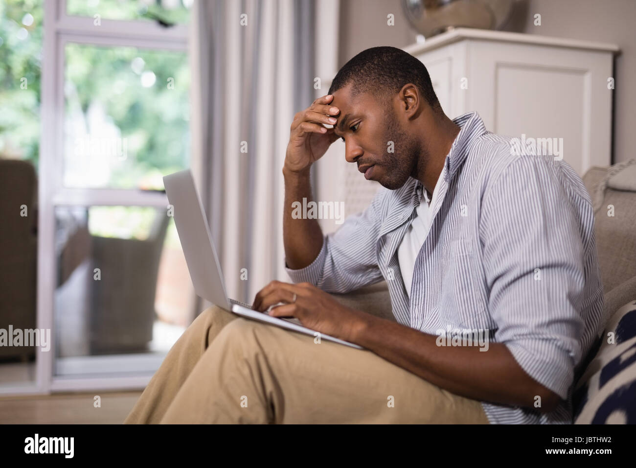 Tensed young man using laptop while sitting at home Stock Photo - Alamy
