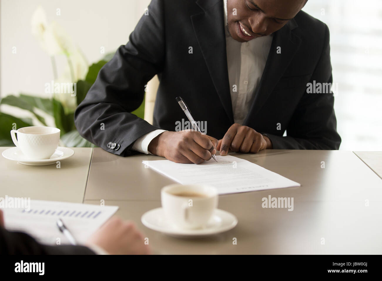 Black afro american young businessman wearing suit puts signature on ...